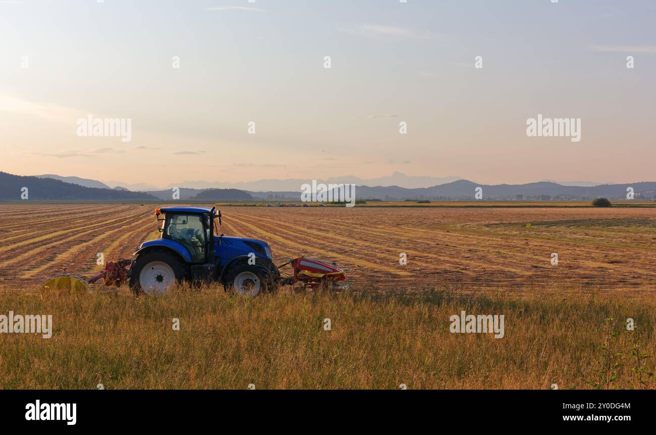 Blue tractor at the edge of an agricultural field at sunset Stock Photo ...