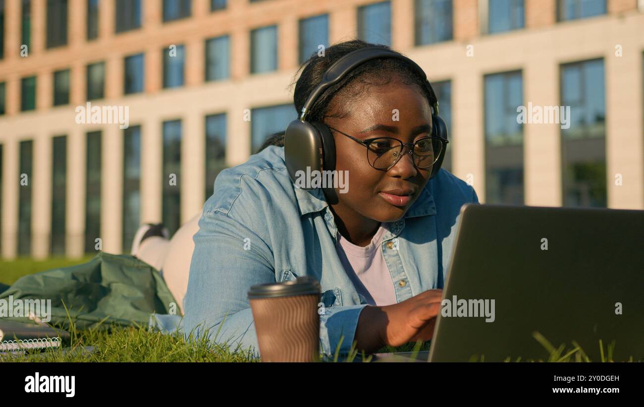 Happy student girl African American woman on lawn lying on green grass ...