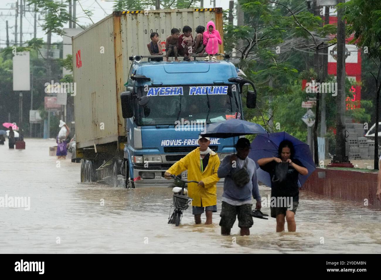 Children ride on top of a truck to avoid floodwaters caused by heavy ...
