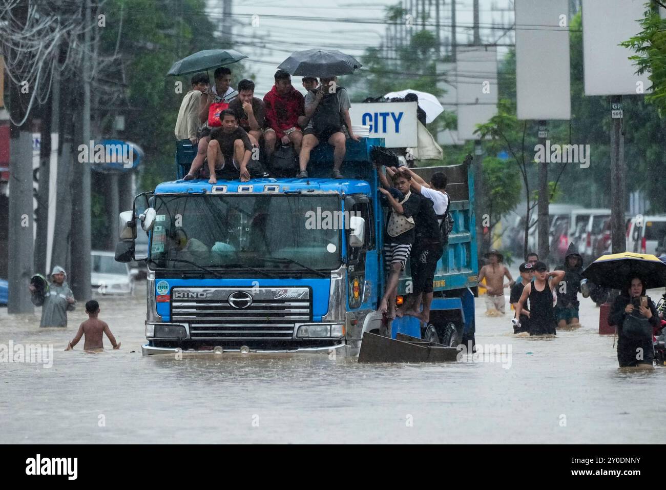 Commuters ride on top of a truck to avoid flood waters caused by heavy ...