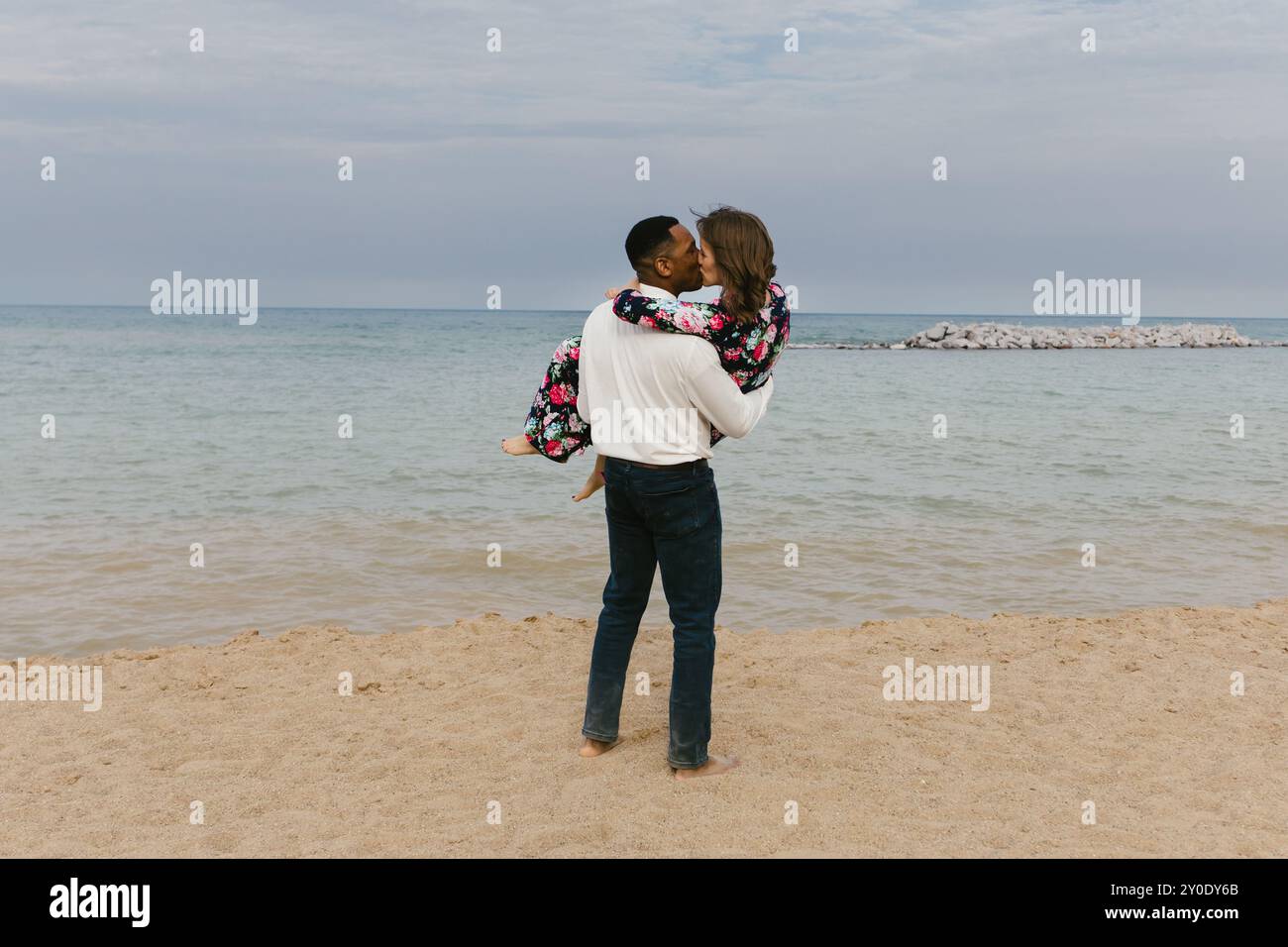 Diverse Husband and wife kiss on beach while in embrace Stock Photo - Alamy