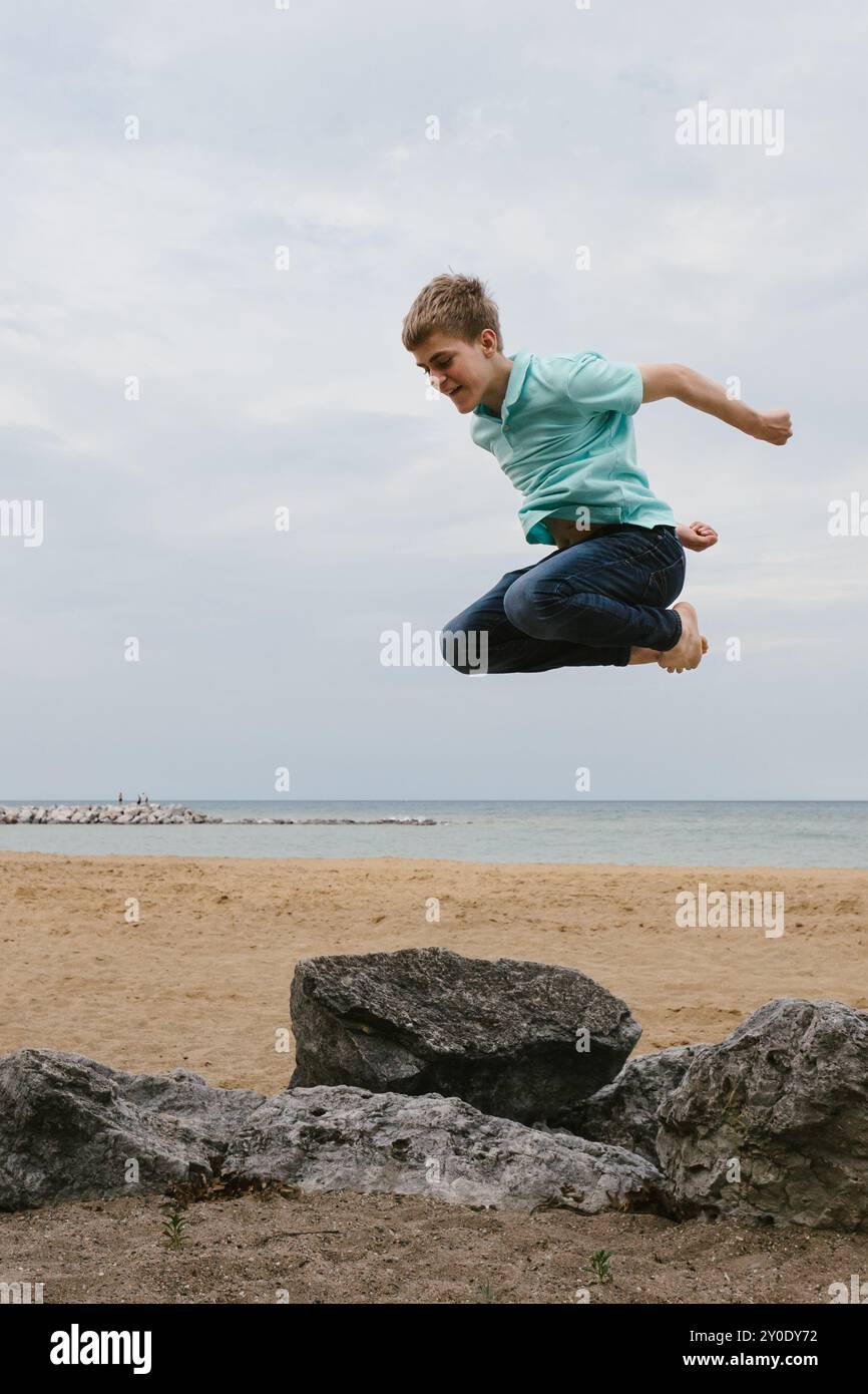 Tween boy jumps off rock into sky on beach having fun Stock Photo - Alamy