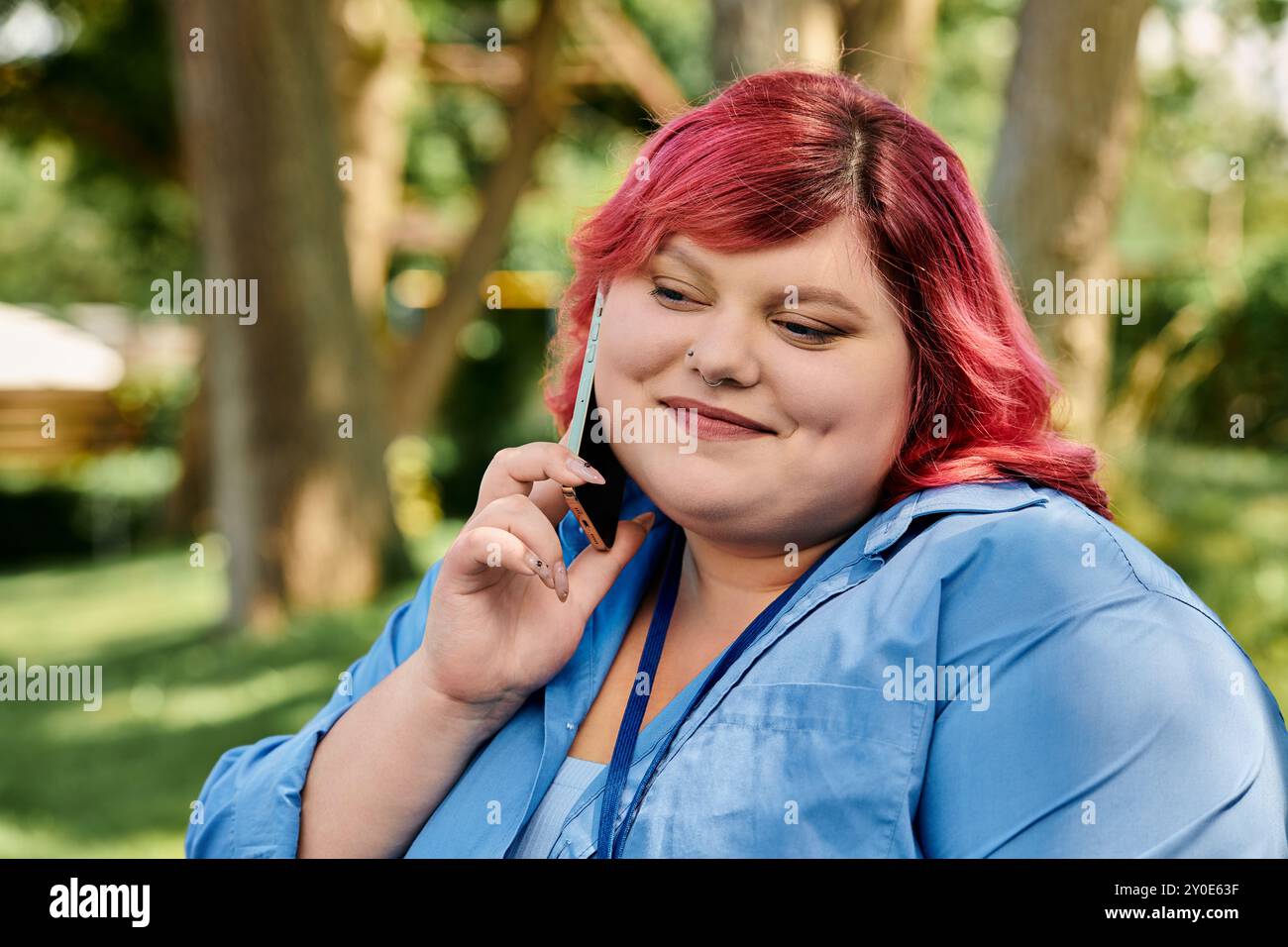 A plus size woman with vibrant pink hair smiles while on a phone call ...