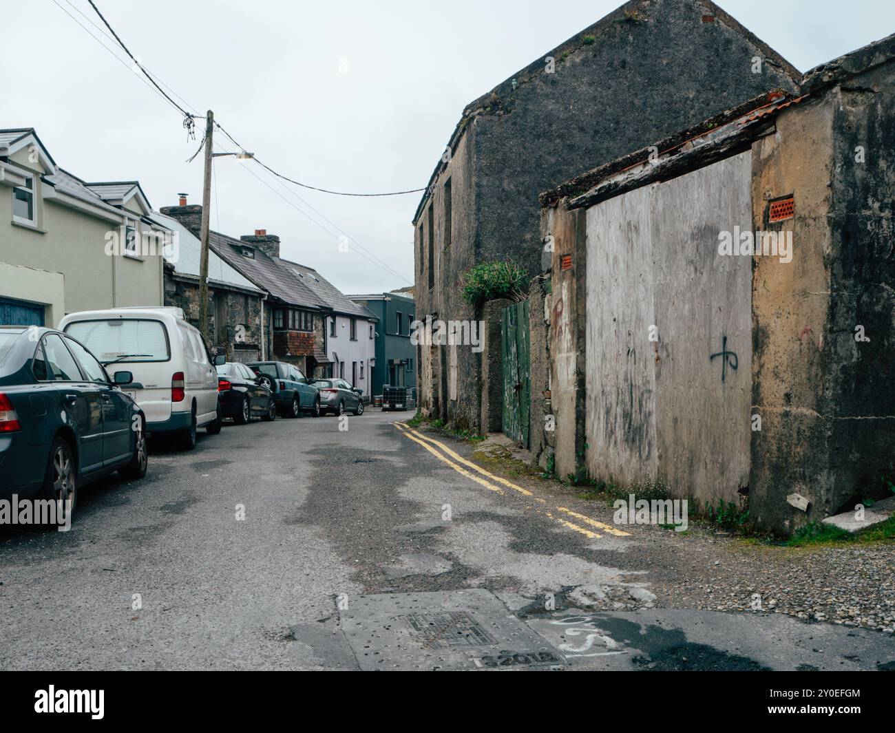 A deserted narrow street features parked vehicles alongside weathered ...