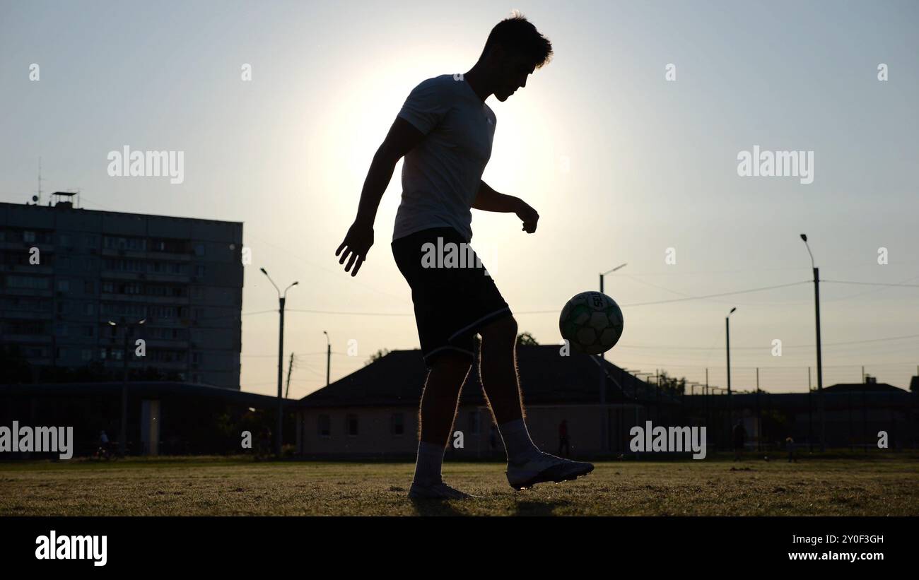 Professional footballer juggling soccer ball on stadium at sunset. Young man kicking ball at green field. Sportsman practicing tricks at meadow with Stock Photo Alamy