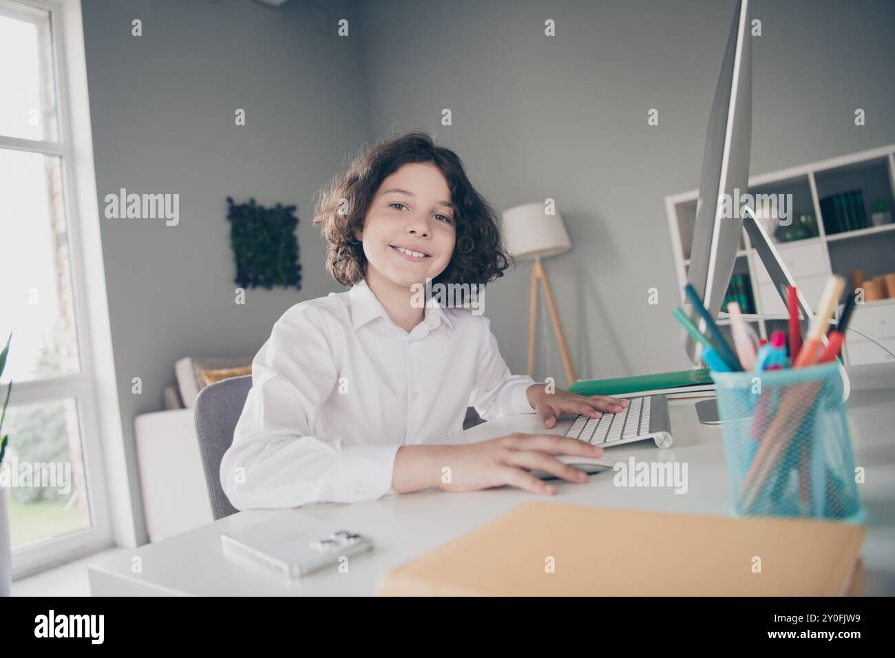 Photo of cute small clever schoolkid wearing white shirt learning from ...