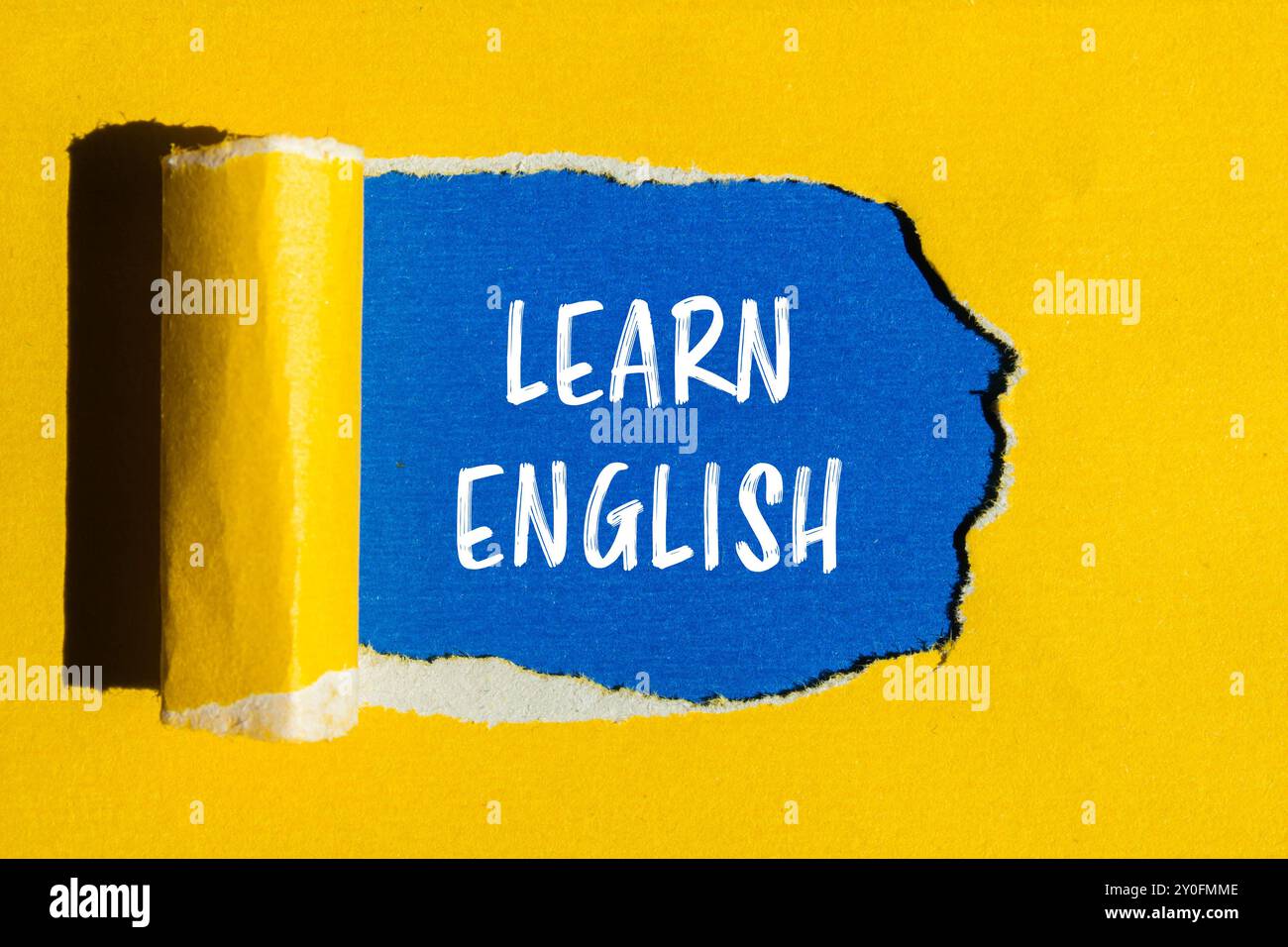 Learn english message written on ripped yellow paper with blue background. Conceptual learn ...