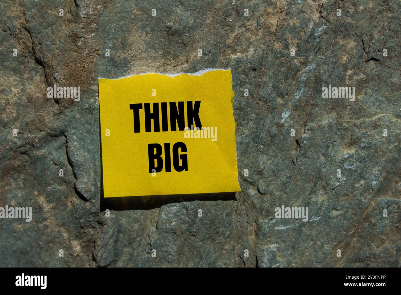 Think big message written on ripped yellow torn paper piece with stone ...
