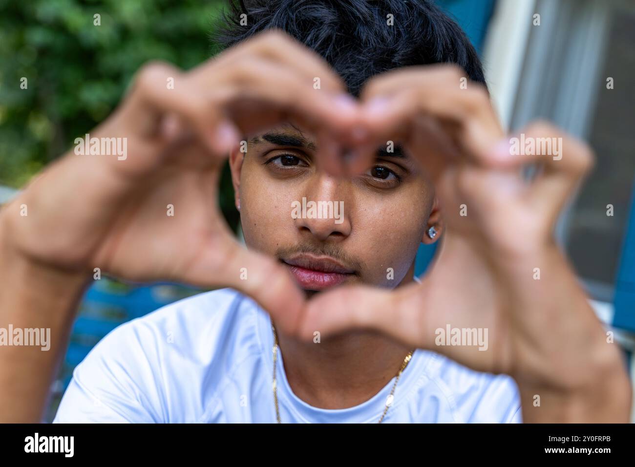 portrait of young teenage man making heart sign with hands outdoors ...