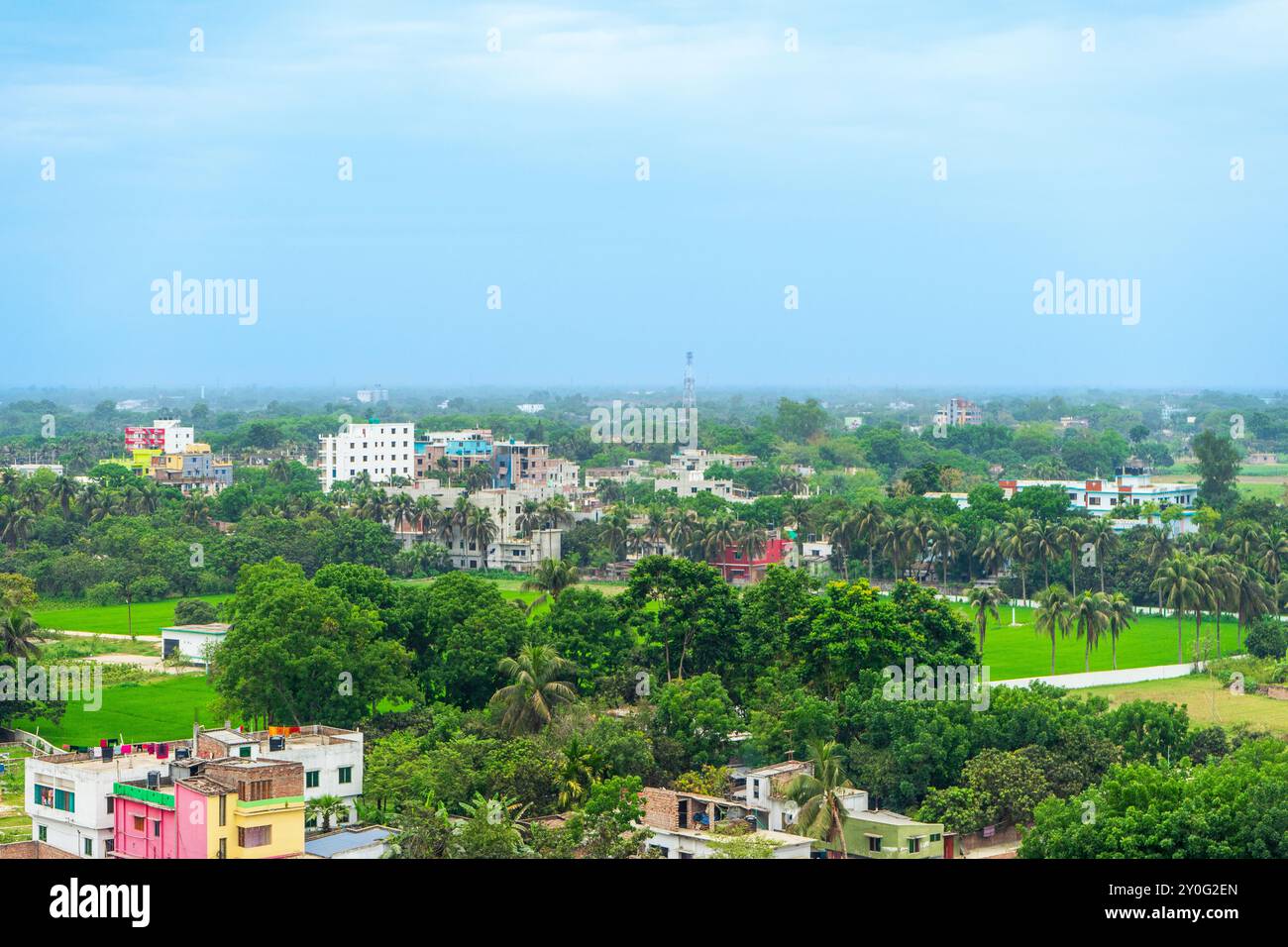 Green landscape with scattered buildings and palm trees under blue sky ...