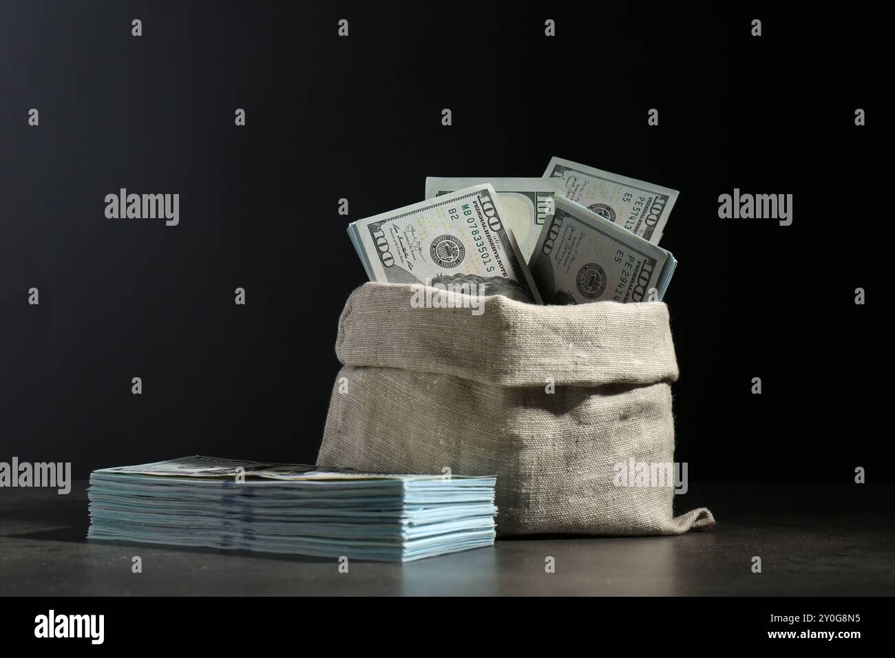 Dollar banknotes in burlap sack on grey table against dark background ...