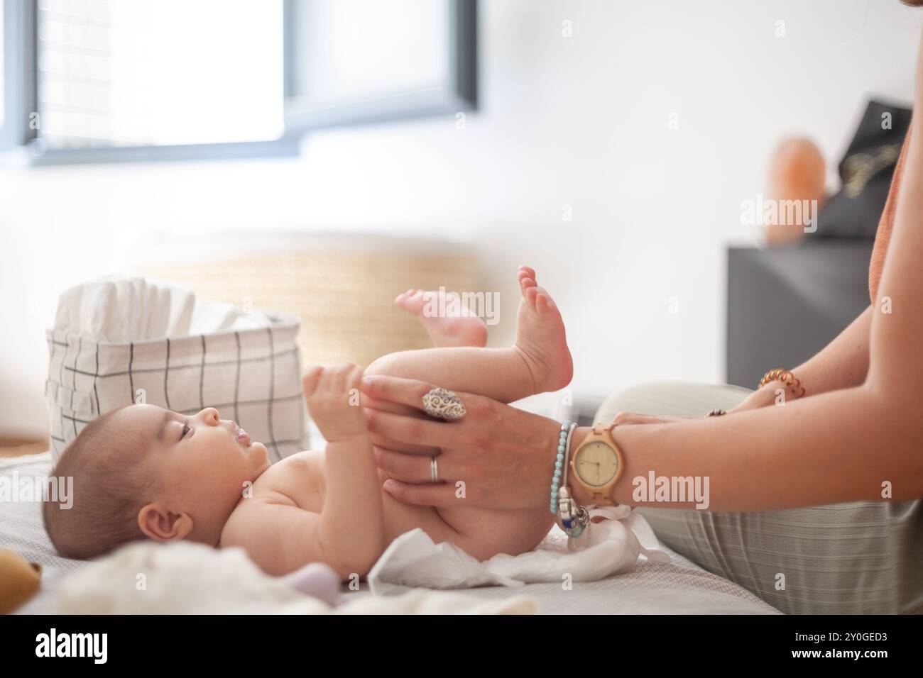 A woman's hands changing a baby's nappy on a bed. Motherhood and family ...
