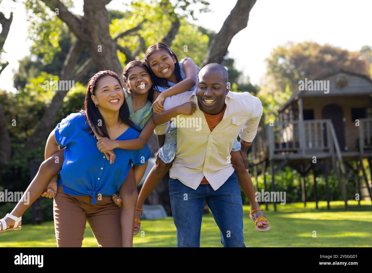 Smiling multiracial parents giving piggyback rides to happy daughters ...