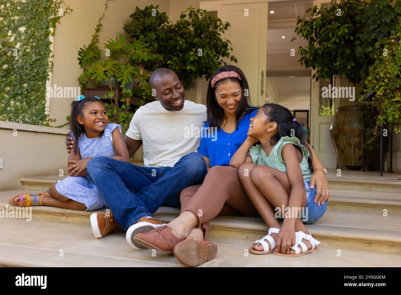 Sitting on steps, happy family of four with daughters enjoying time ...