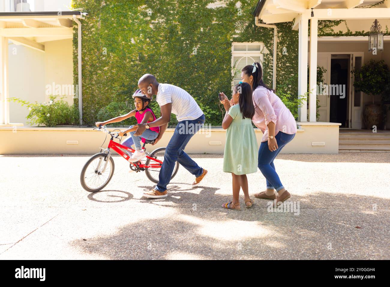 Teaching child to ride bicycle, parents and siblings cheering in front ...