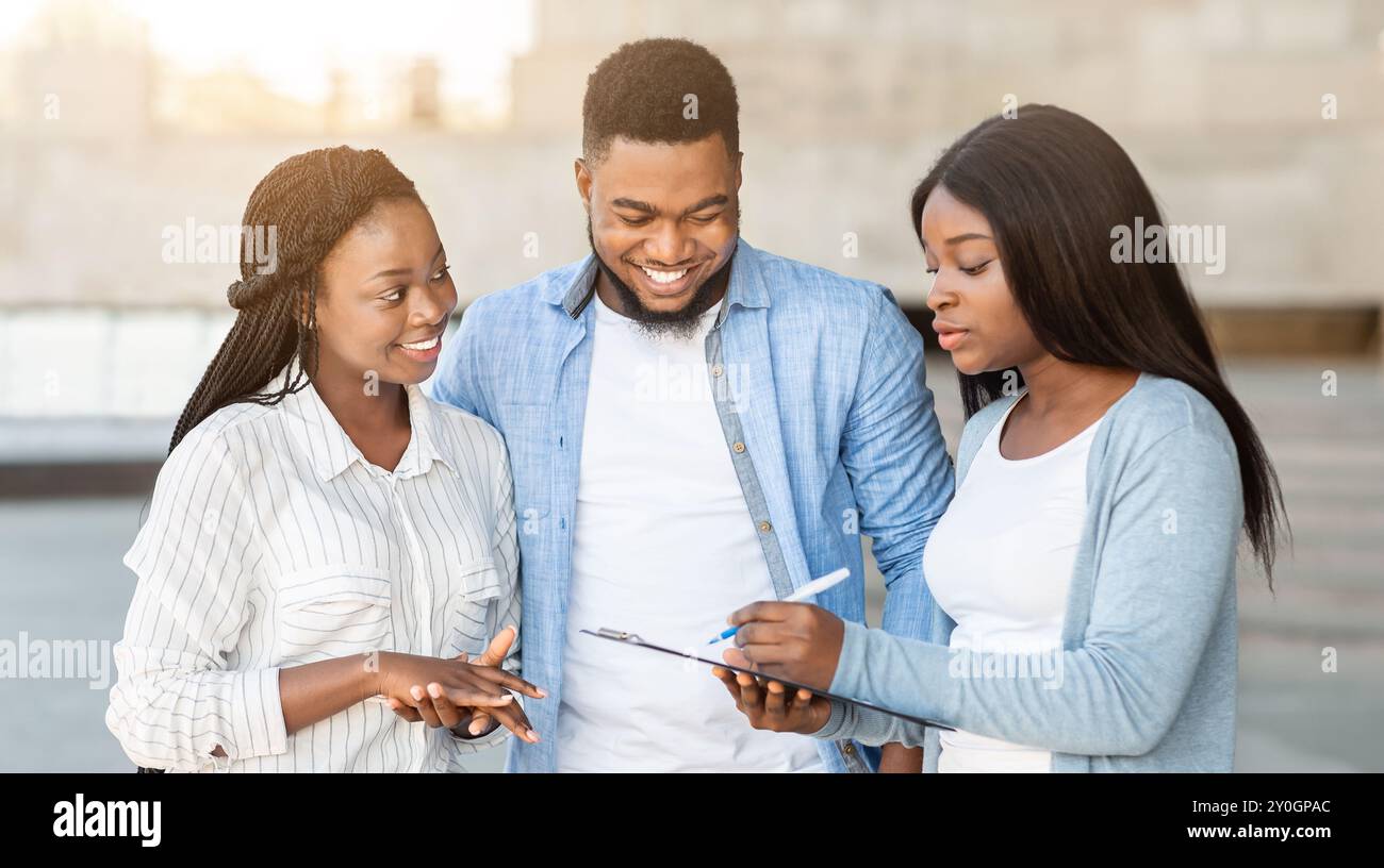 Afro woman interviewing young couple, conducting survey in the street ...