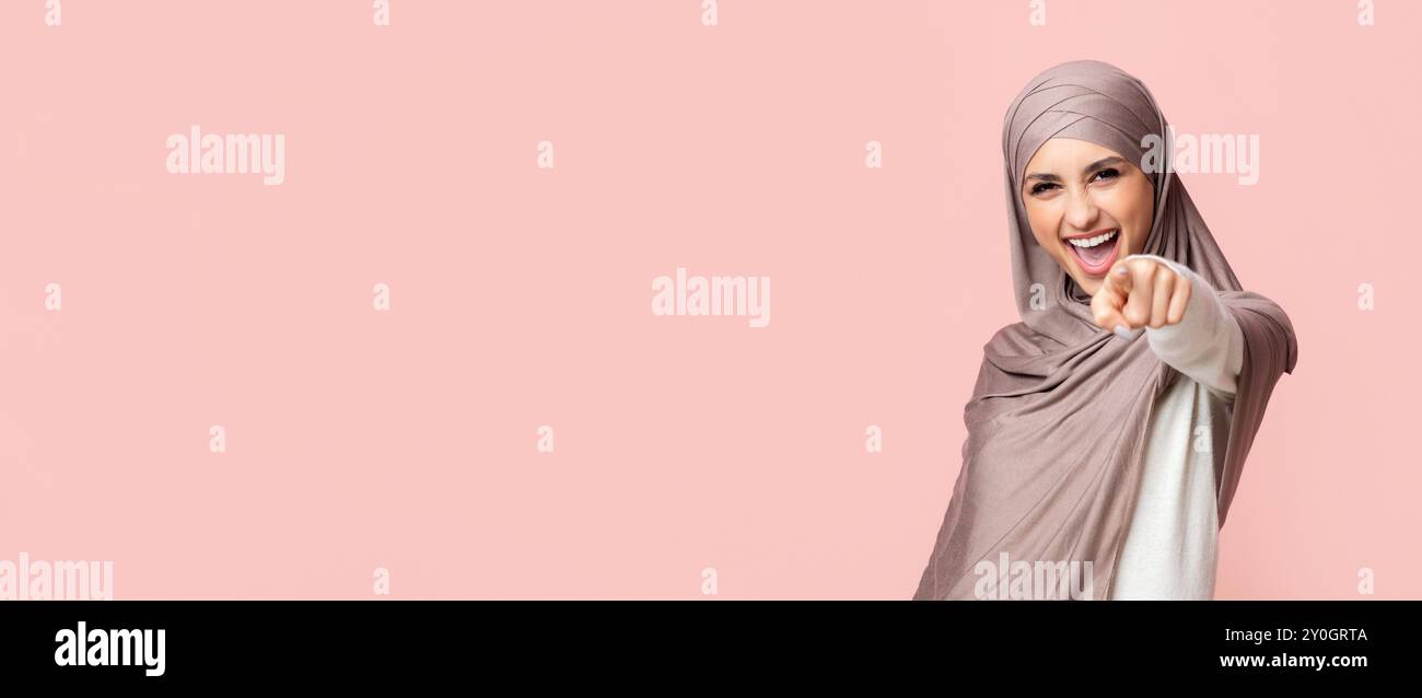 Arabic woman laughing and pointing finger at camera over pink ...