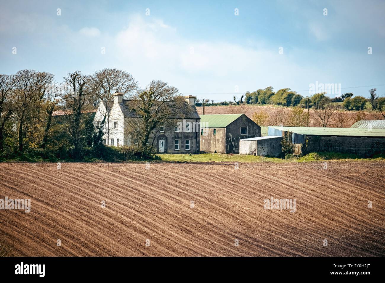 A two-story house with a green roof sits next to a larger building with ...