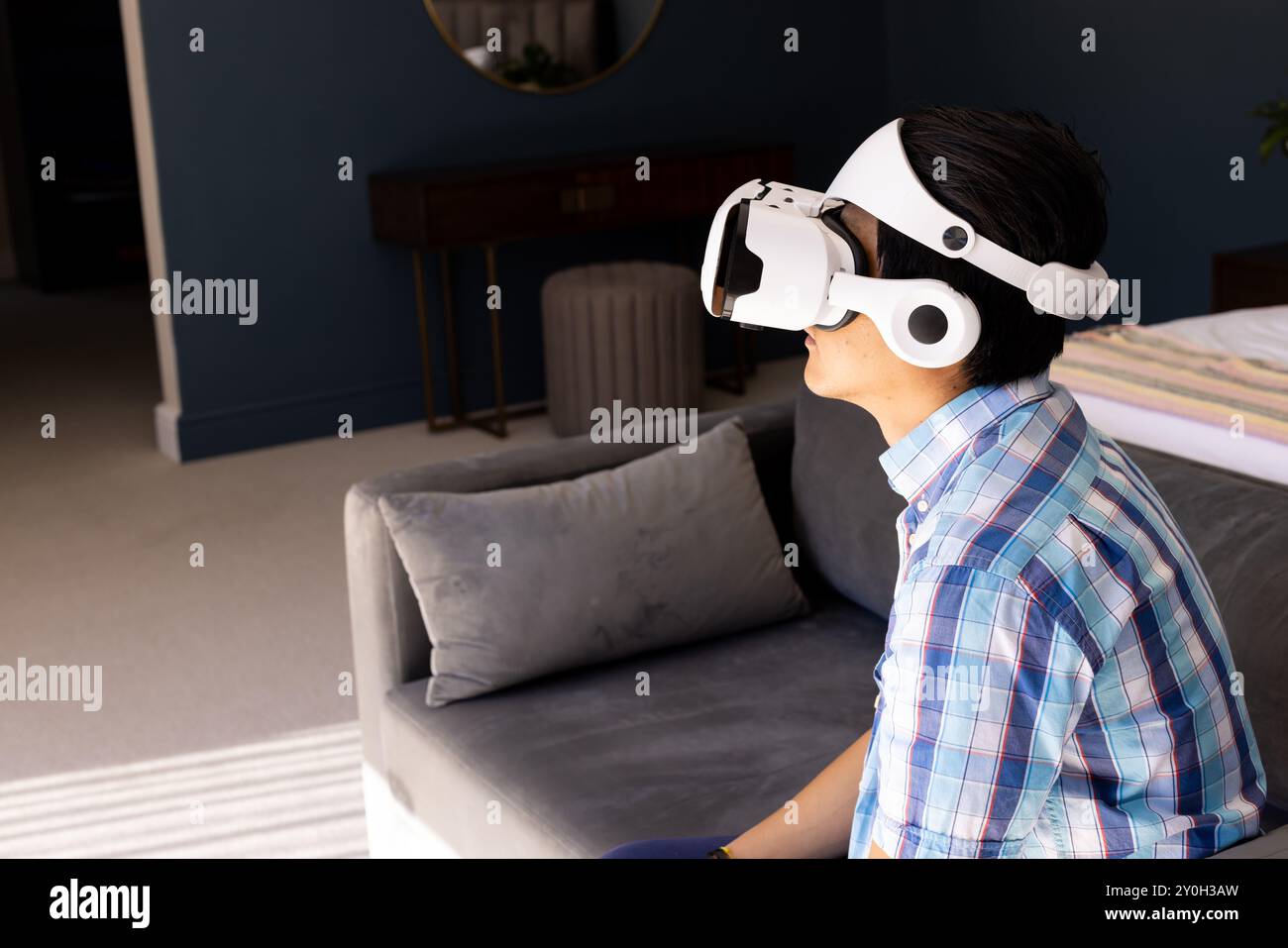 Using VR headset, asian man sitting on couch in modern living room ...