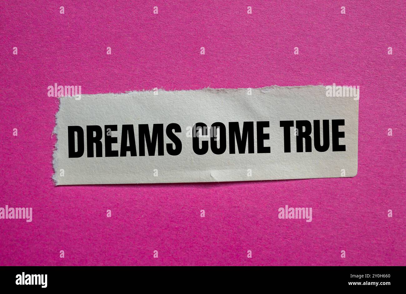 Dreams come true message written on ripped torn paper piece with pink ...