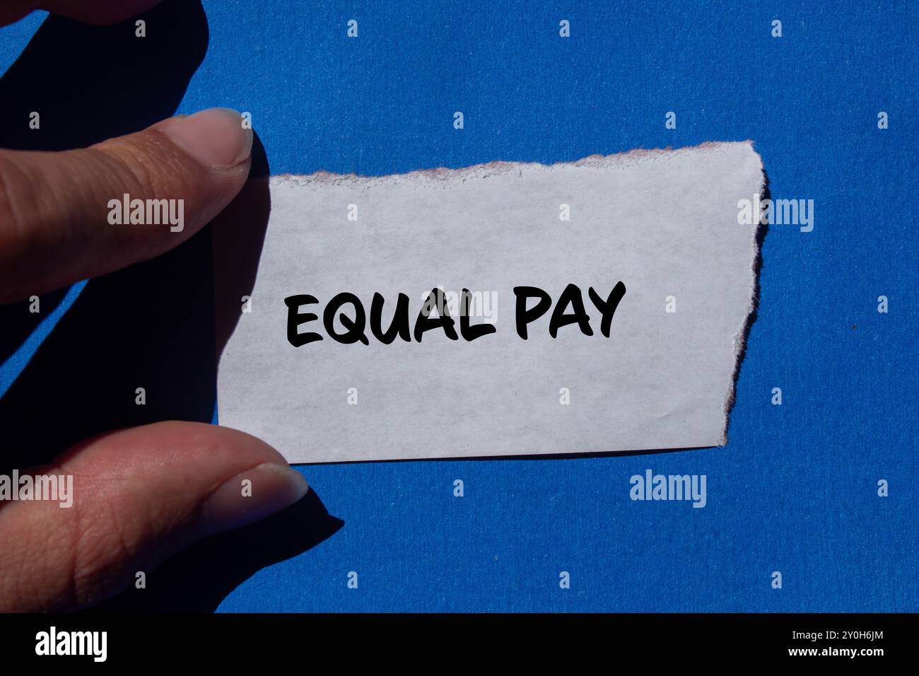 Equal pay message written on ripped torn paper with blue background ...