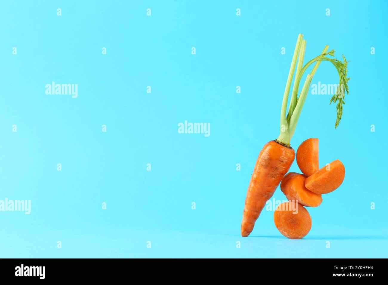 Whole and cut fresh carrots on light blue background, space for text ...