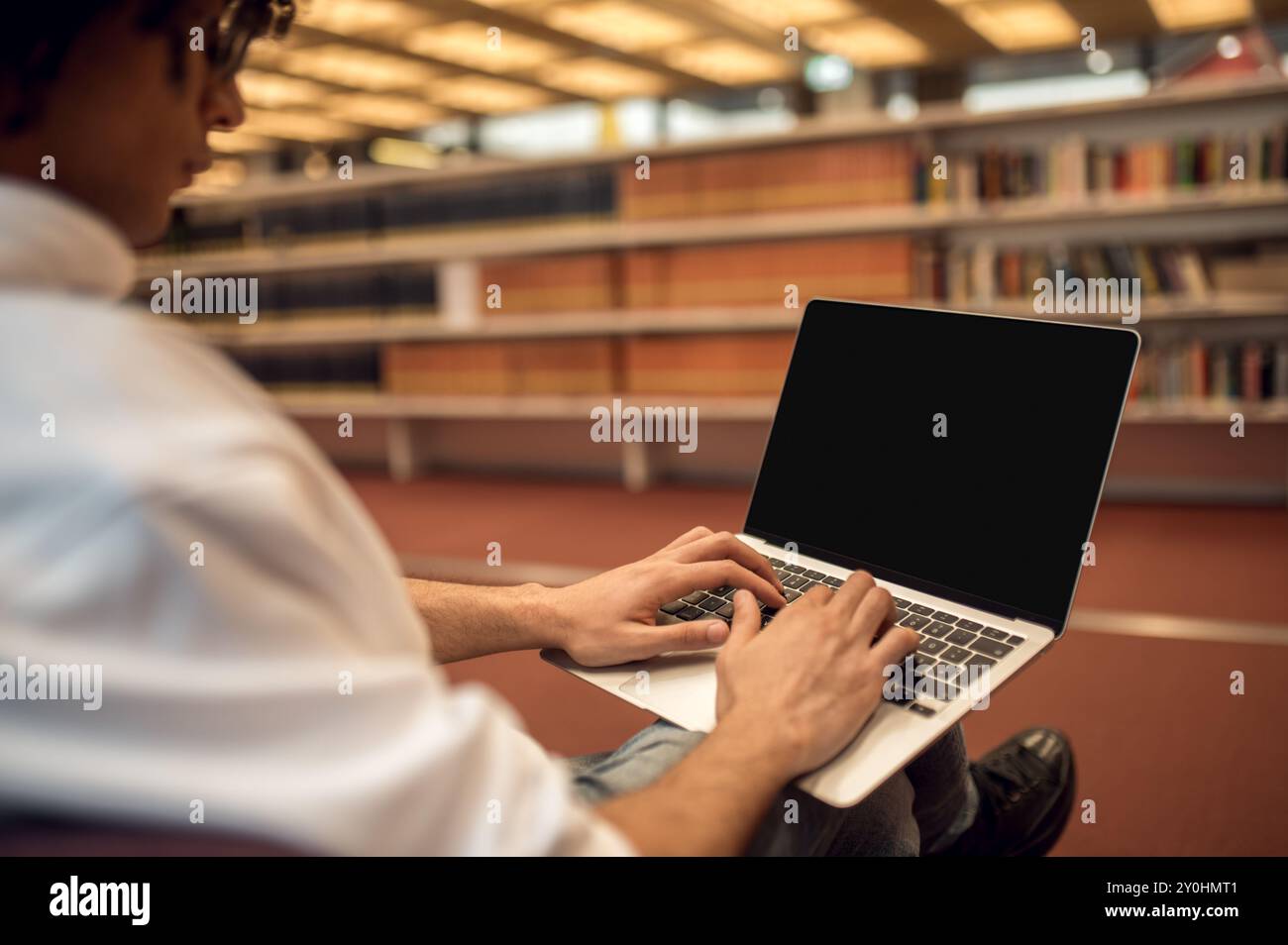 Young male student embracing technology for studying in library Stock ...