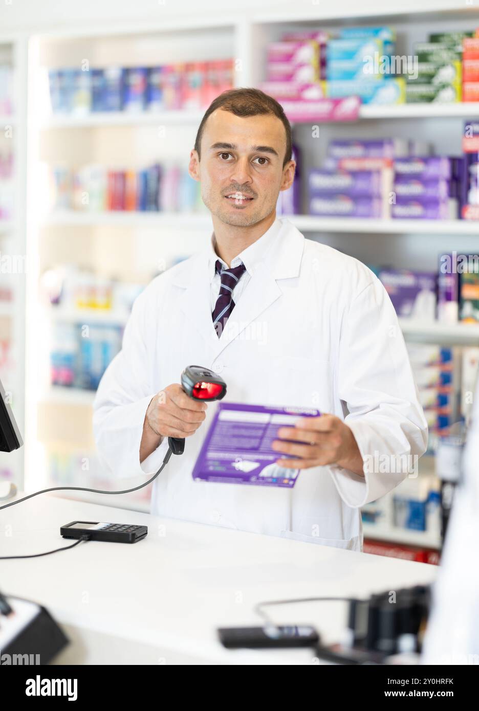 Man pharmacist in cash area works with computer and goods, scans drugs ...