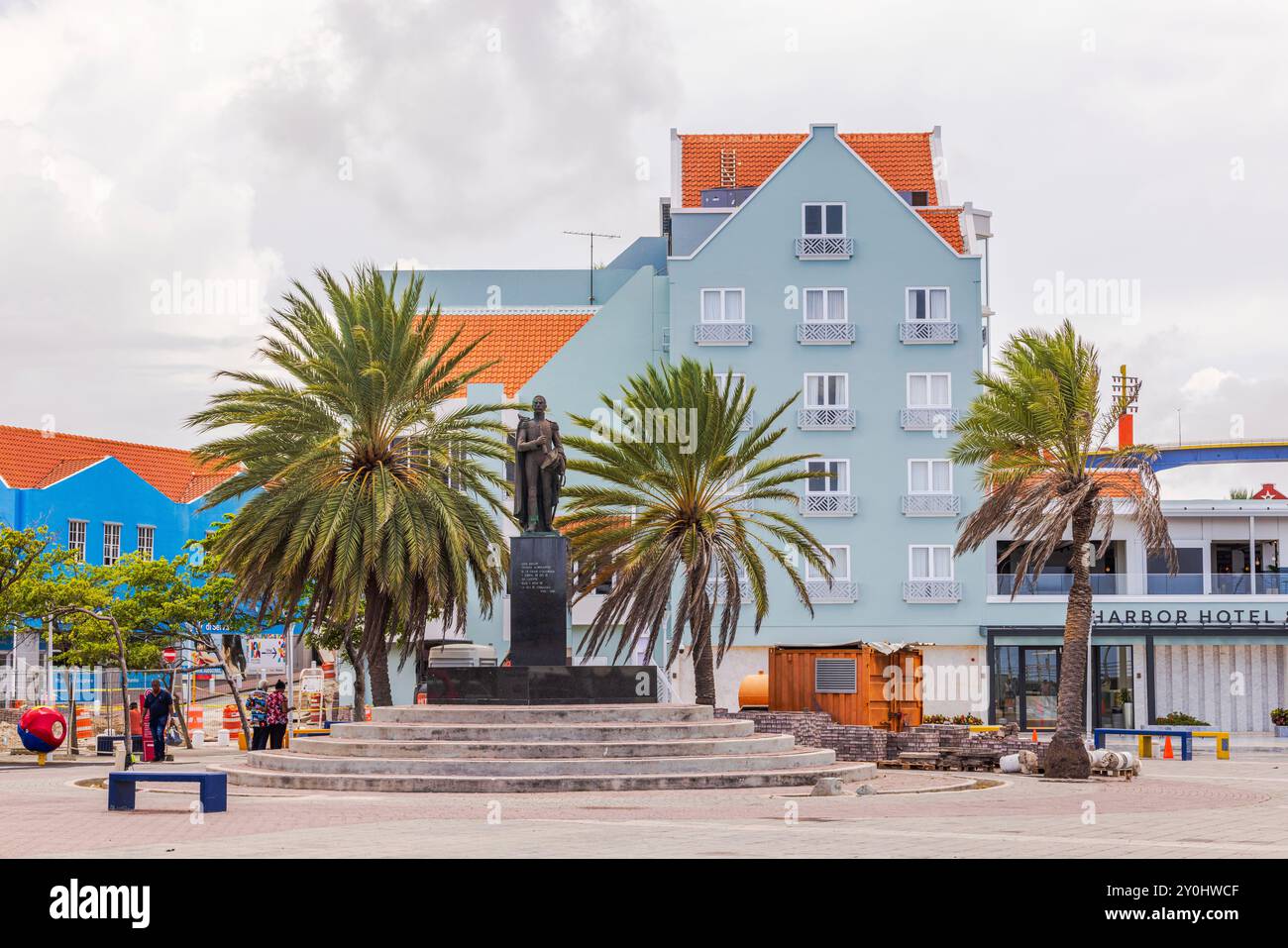 View of public square with statue, palm trees, and colorful buildings ...