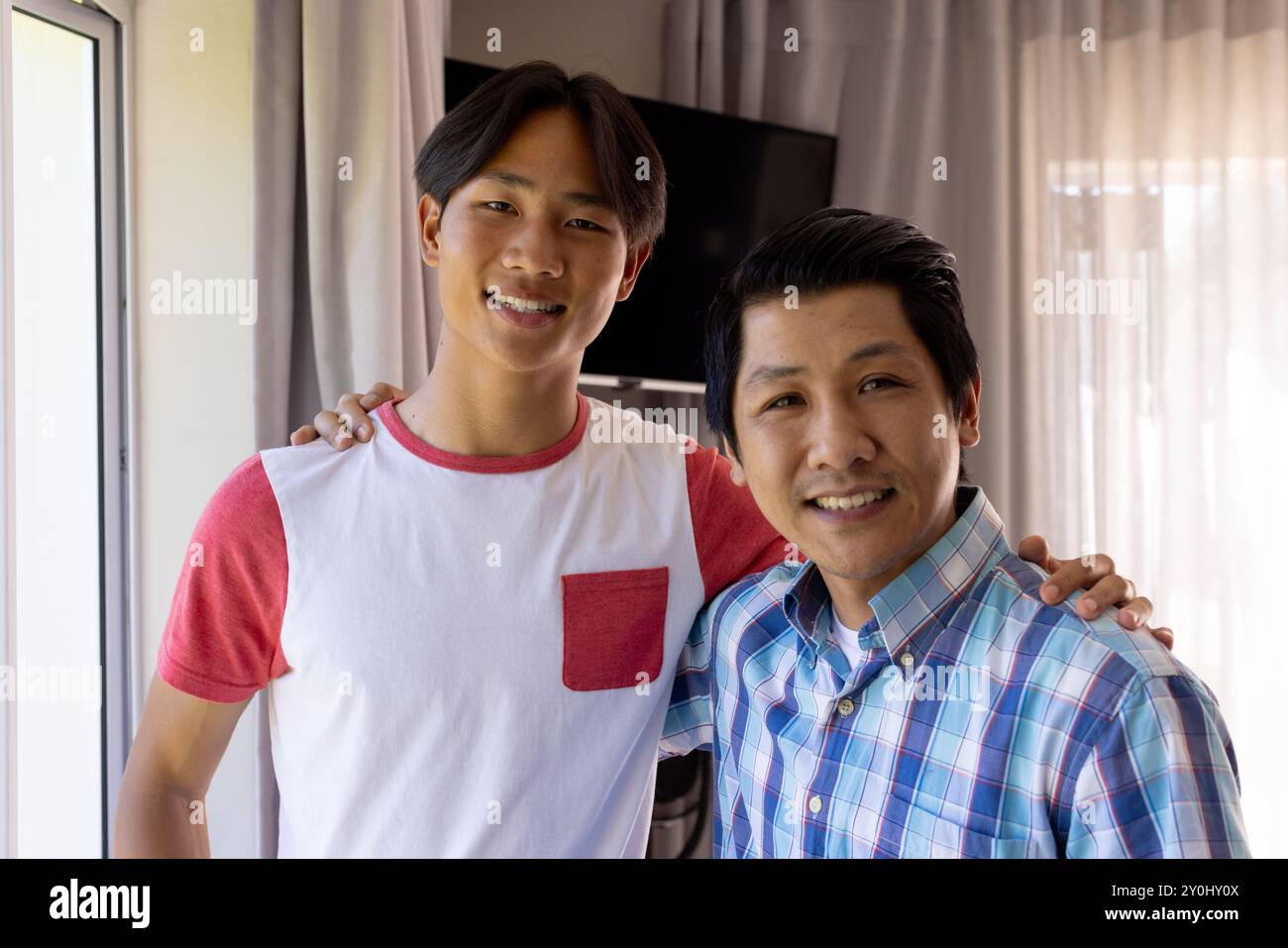 Smiling Asian father and teenage son standing together indoors ...