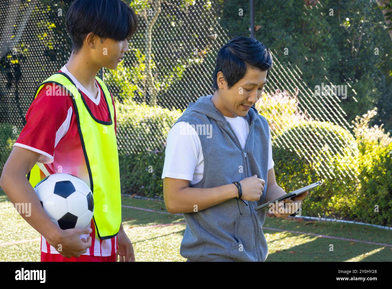 Coach using tablet to discuss strategy with teenage male soccer player ...