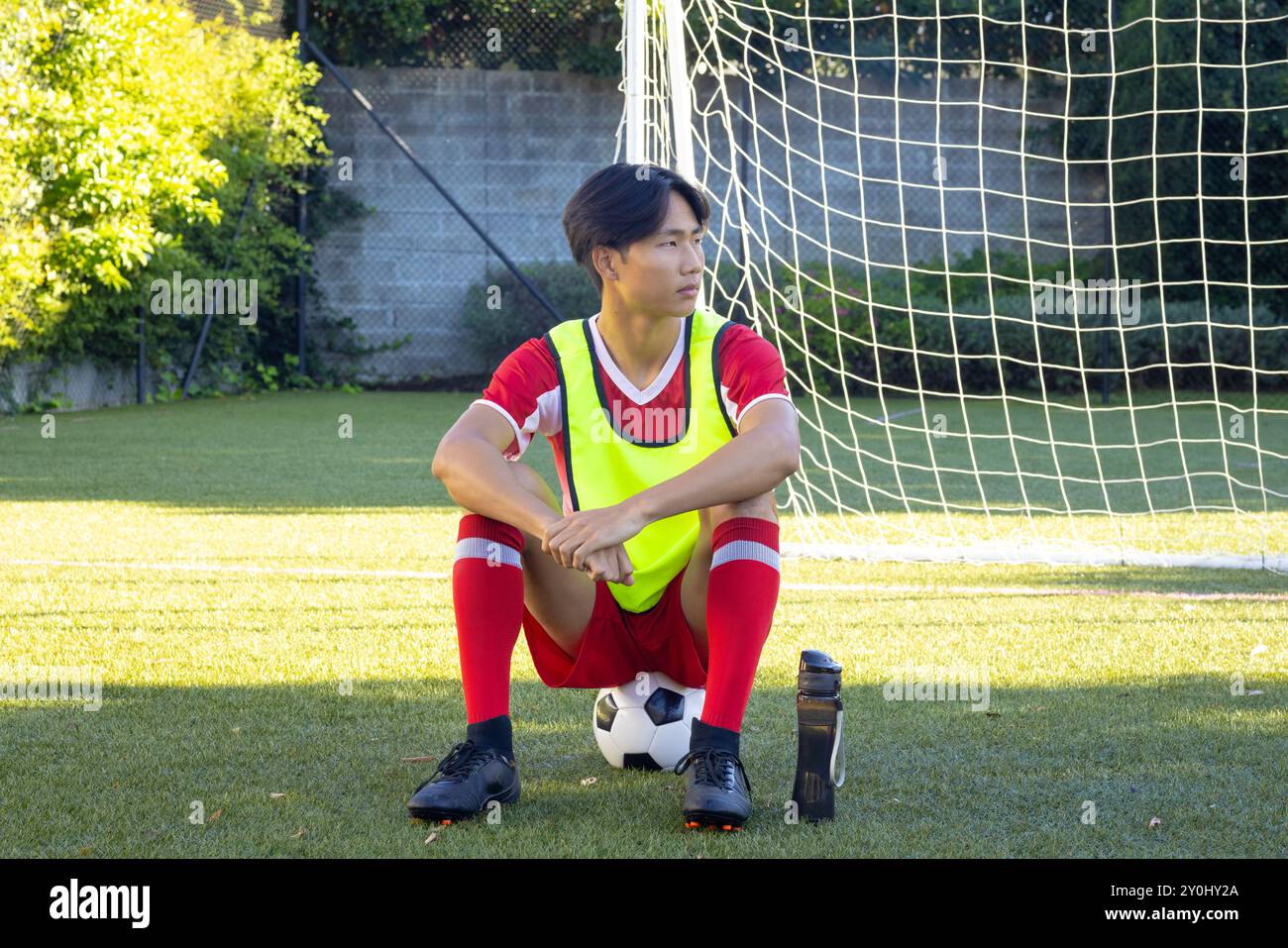 Resting on soccer field, athlete in uniform with soccer ball and water ...