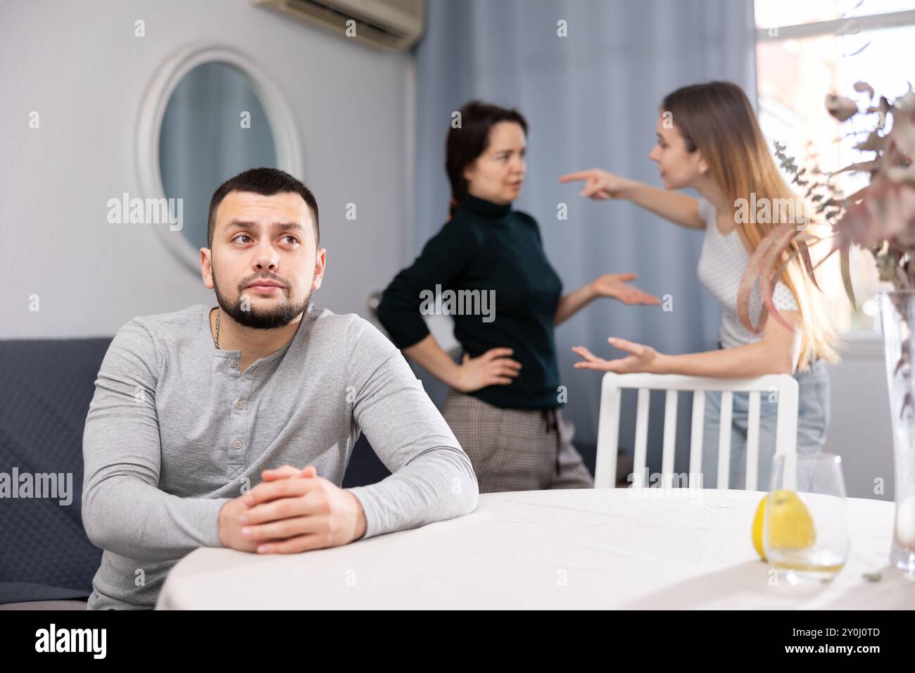 Depressed man sitting at table while two women arguing Stock Photo - Alamy