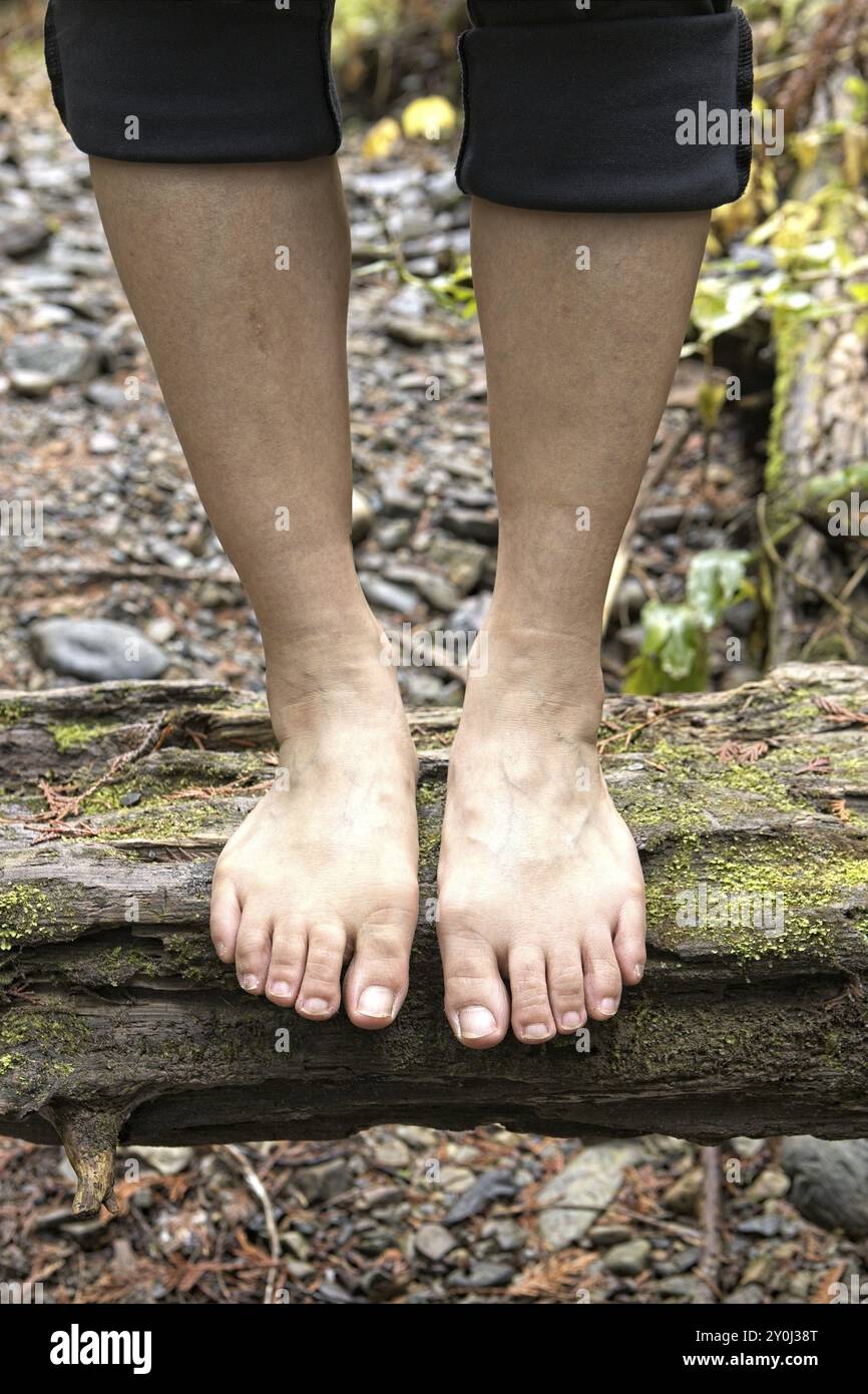 A close up of a womans legs and feet standing on top of a log in nature ...