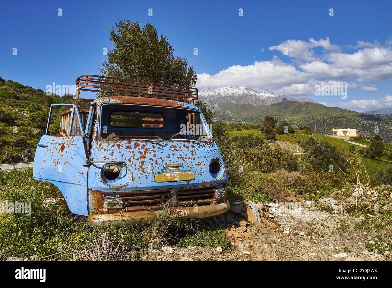 Abandoned rusty blue car on a green field with mountains in the ...