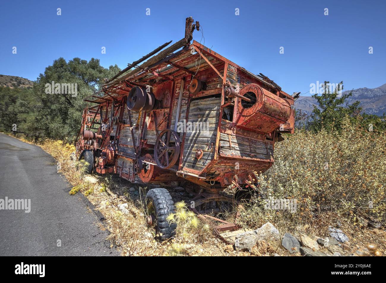 Dilapidated, rusted combine harvester next to the road under blue sky ...