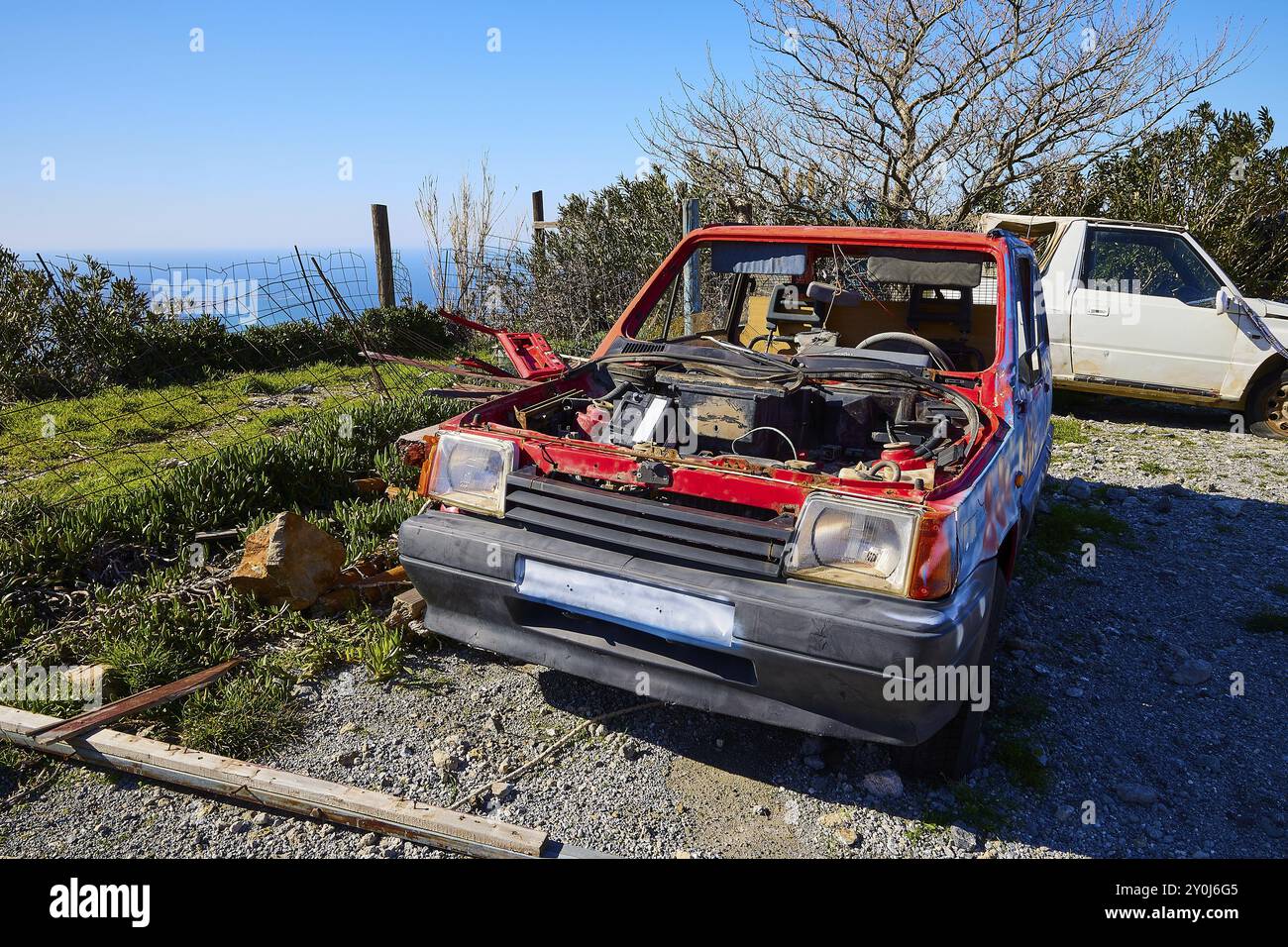 An abandoned, red car without bonnet overlooking the sea, wrecked ...