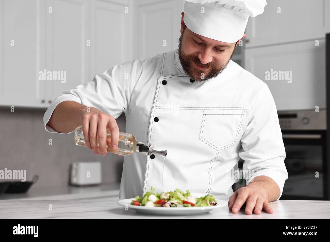 Professional chef pouring oil onto delicious salad at white marble ...