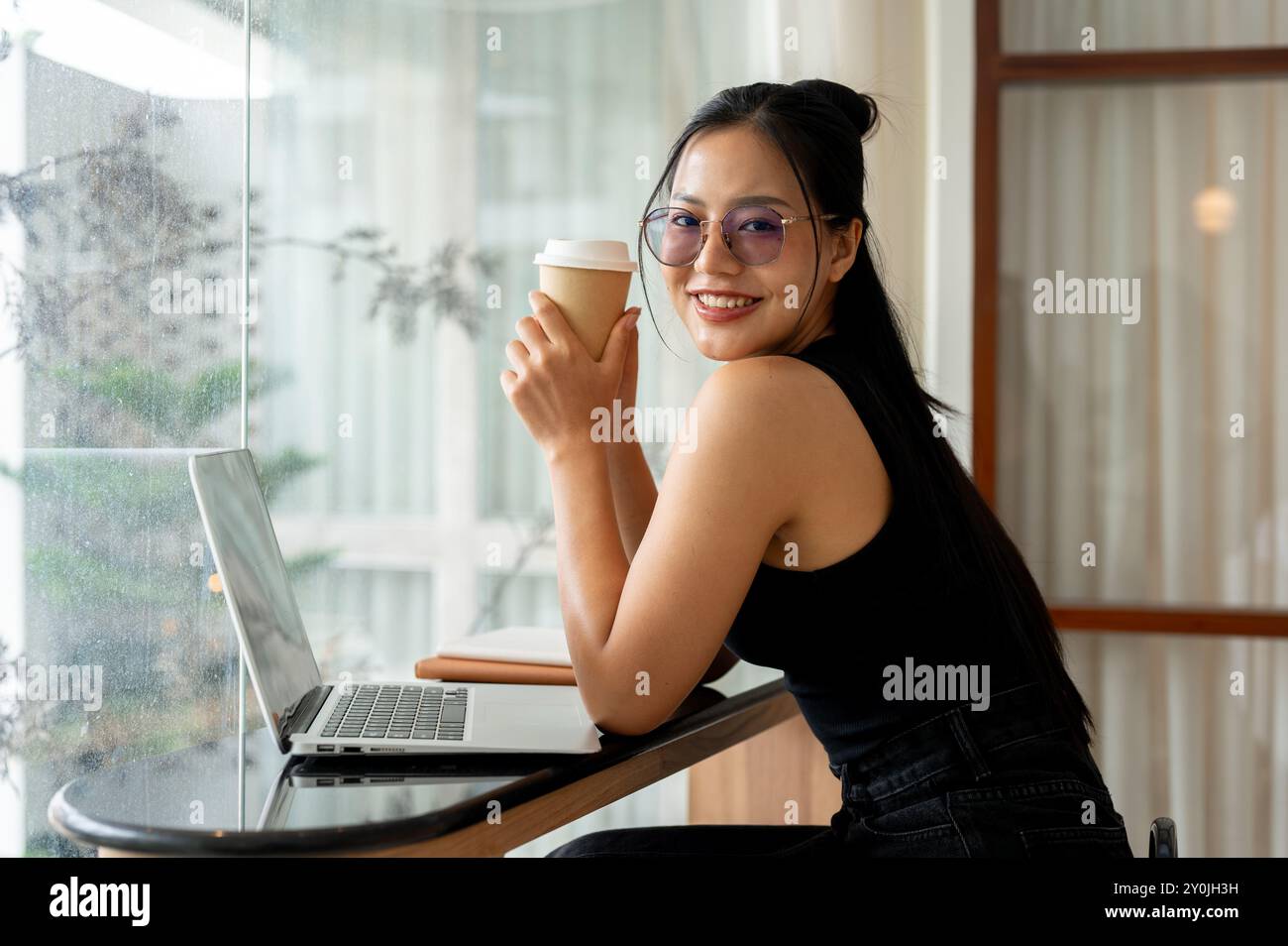 An attractive, fashionable Asian woman working remotely from a coffee ...