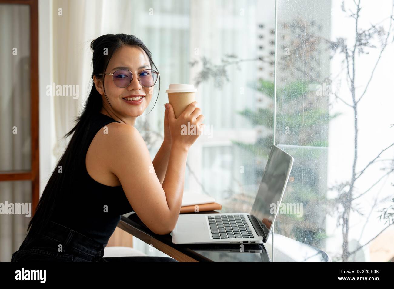 An attractive, fashionable Asian woman working remotely from a coffee ...