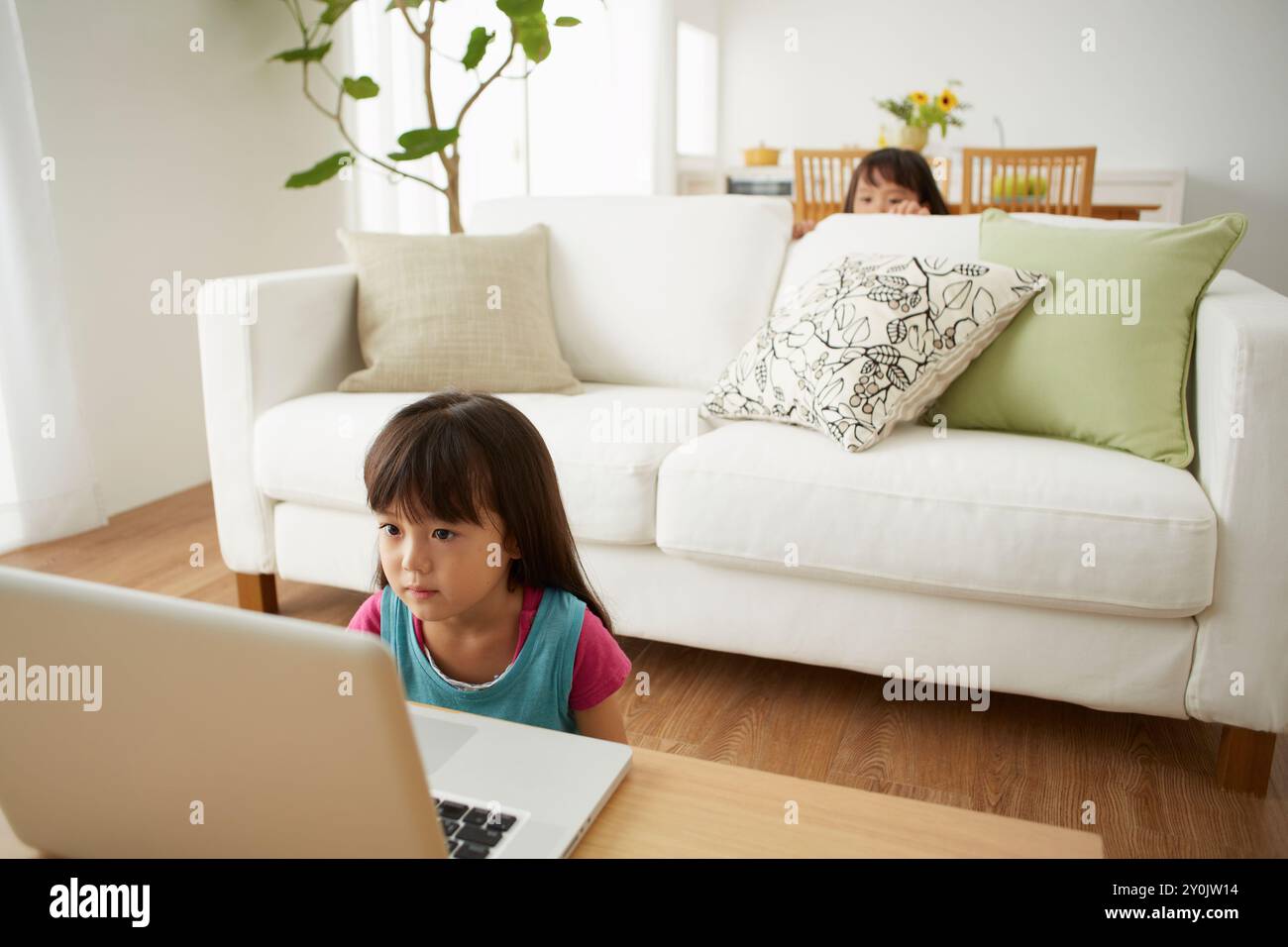 Girl looking at a computer on the living table and her brothers looking ...