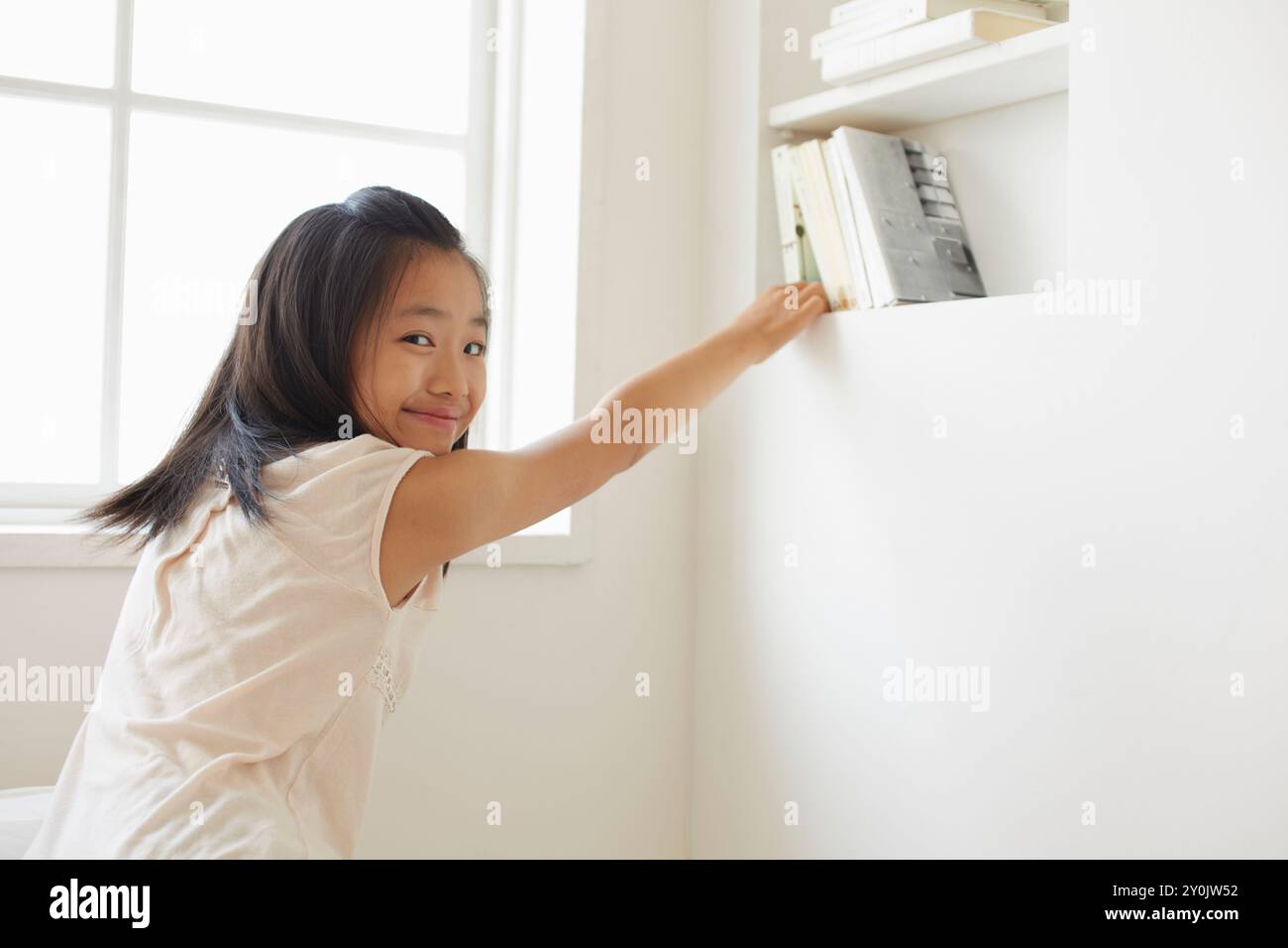 Girl taking books out of a bookcase by the window Stock Photo - Alamy
