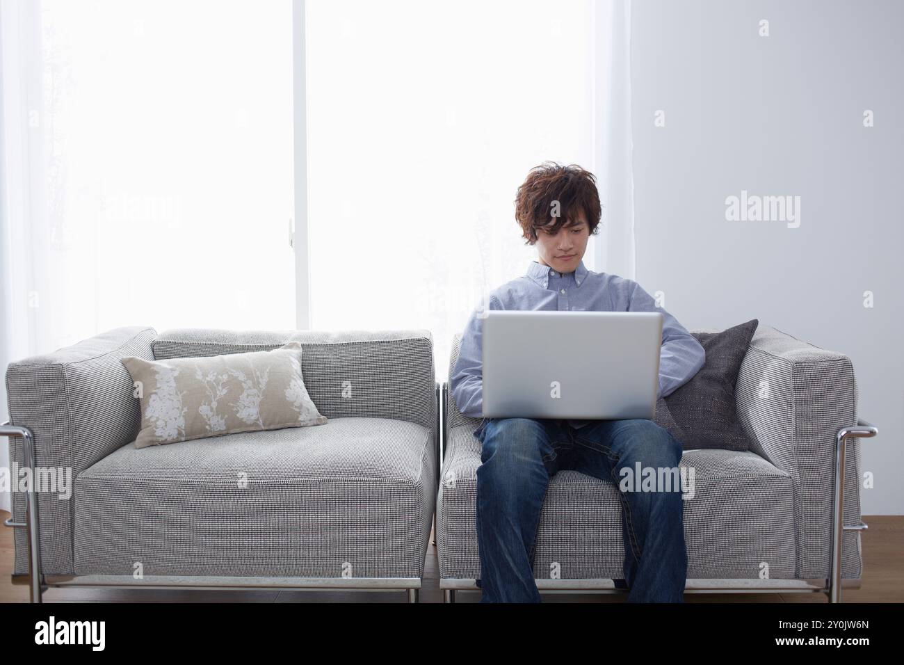 Man sitting on the living room sofa and placing a computer on his legs ...