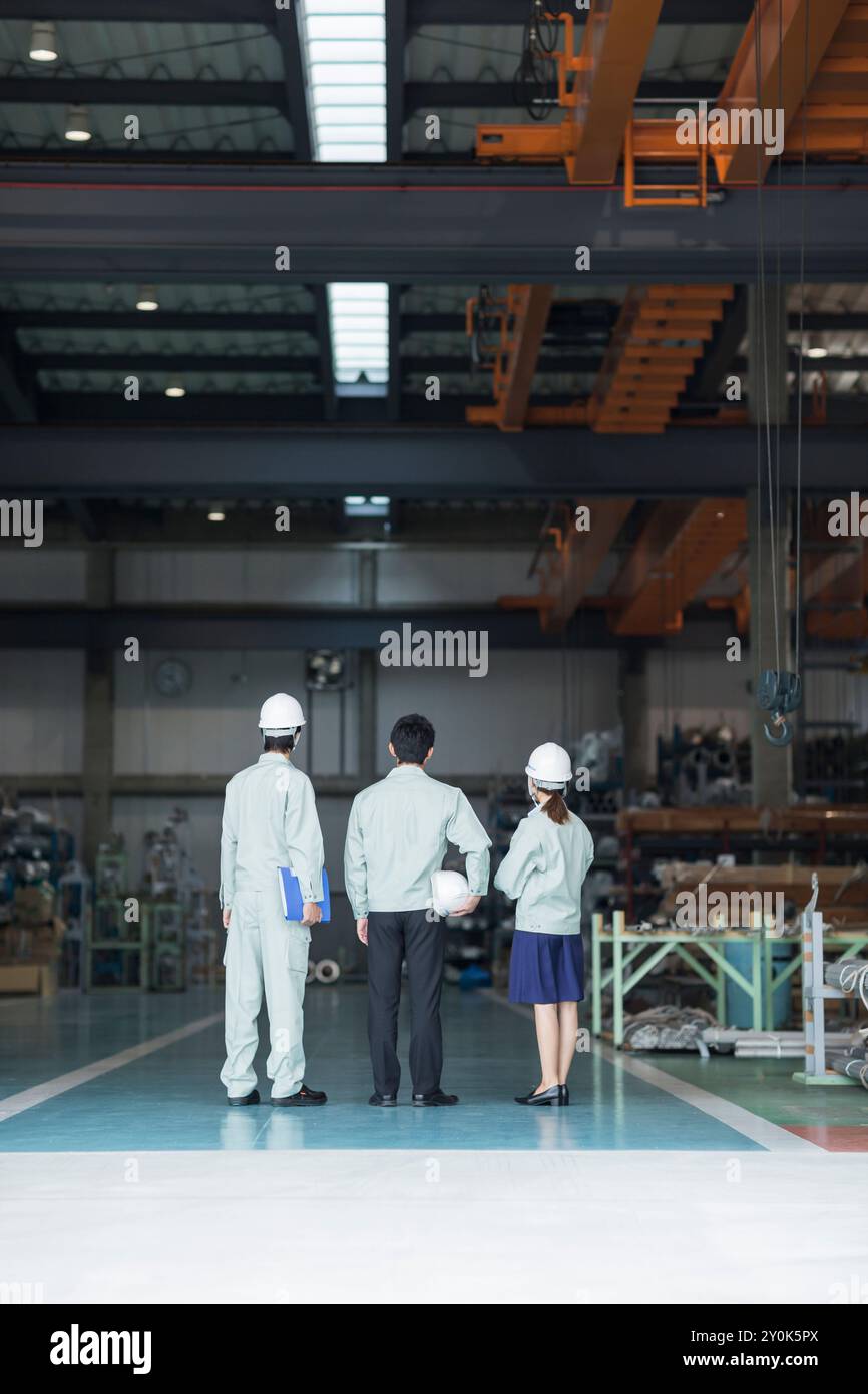 the back view a pair of male and female workers standing in a factory ...