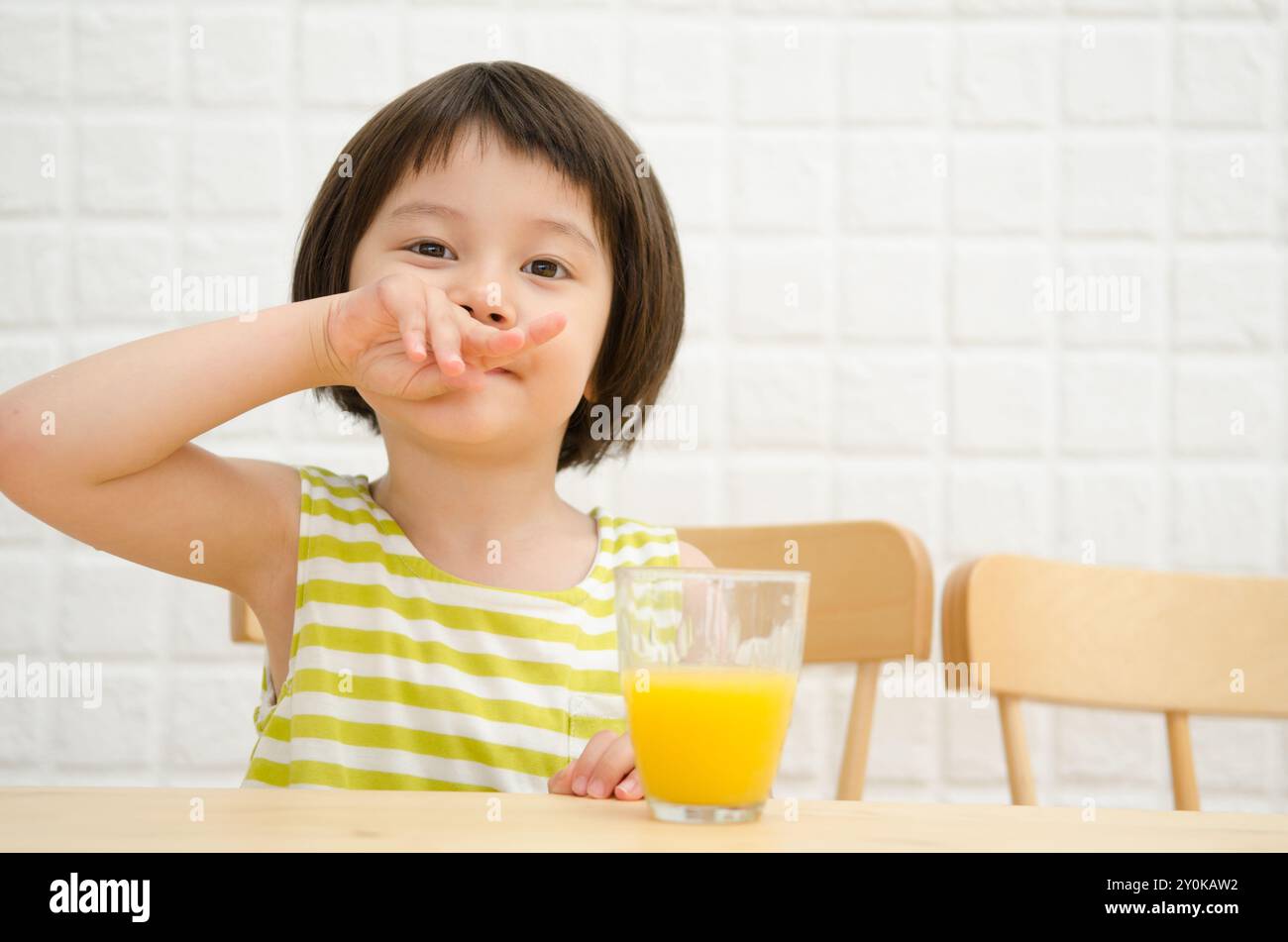 Girl rubbing her nose sitting on a chair Stock Photo - Alamy