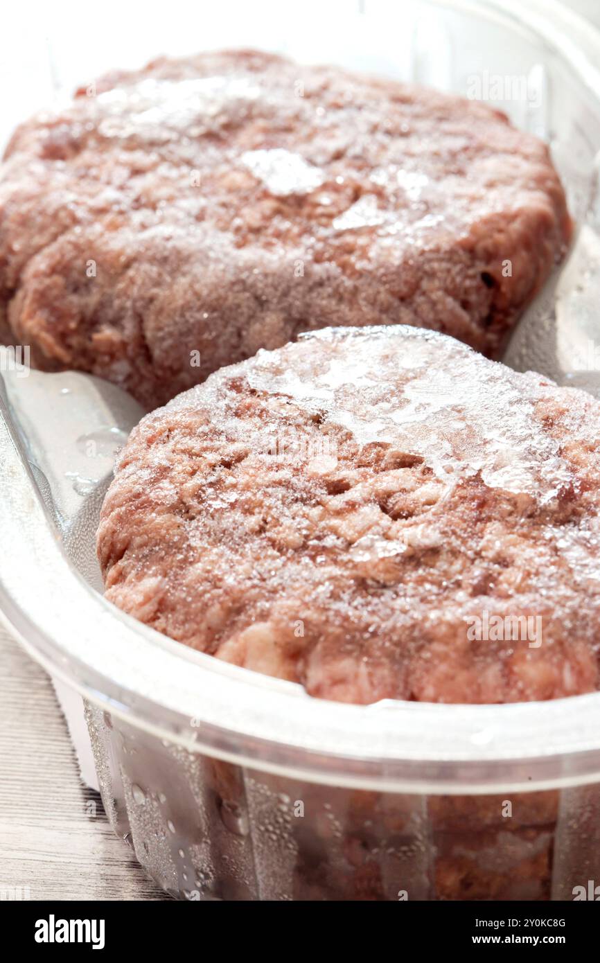 Frozen beef burgers in plastic tray packaging thawing. On a grey wood ...