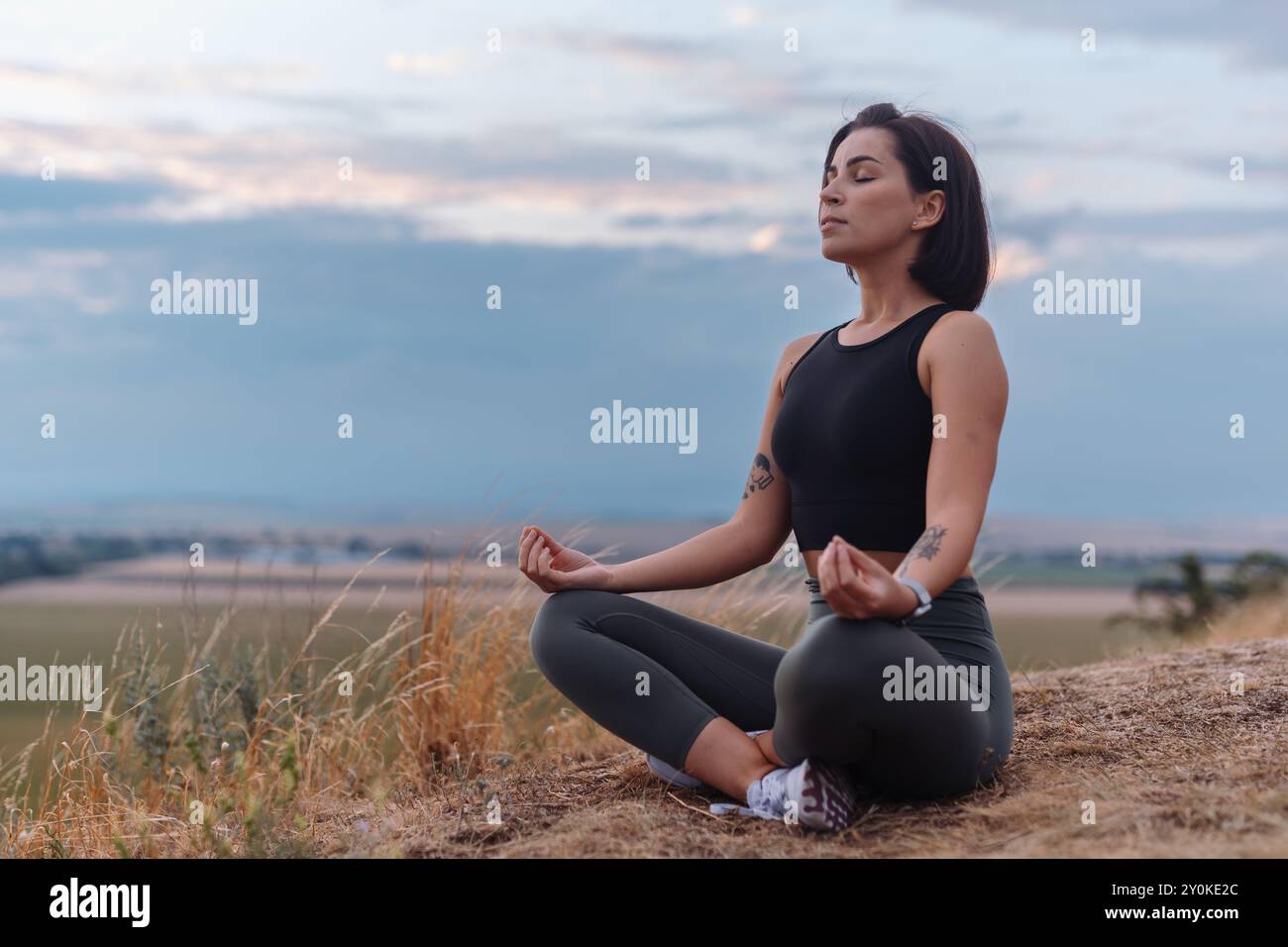 A serene woman meditates outdoors in nature at sunset, embracing ...