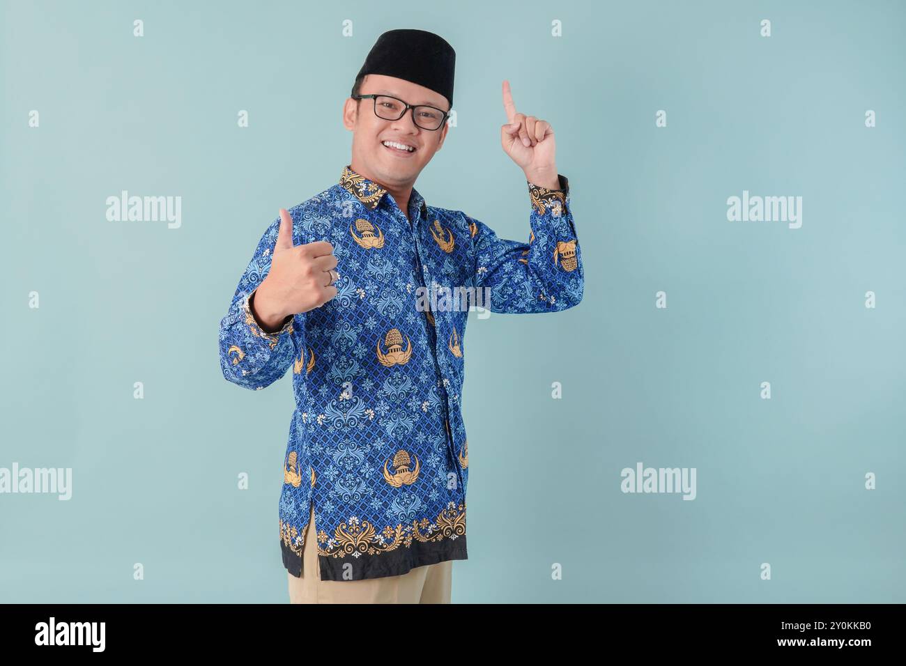 Cheerful government worker man wearing blue batik uniform pointing to ...