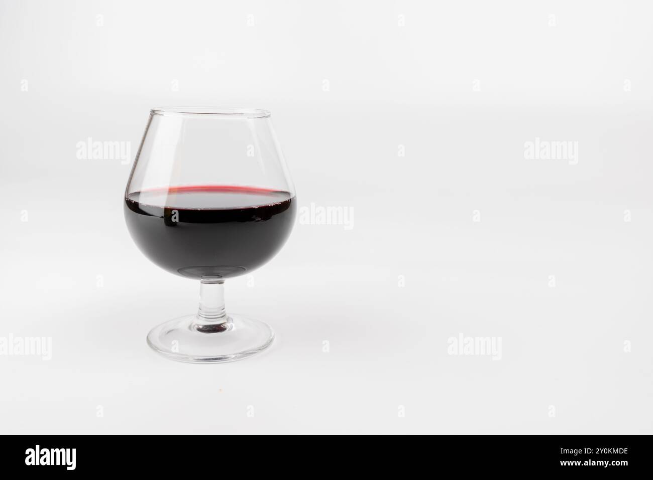 A horizontally aligned photo showing a wine glass filled with red wine ...
