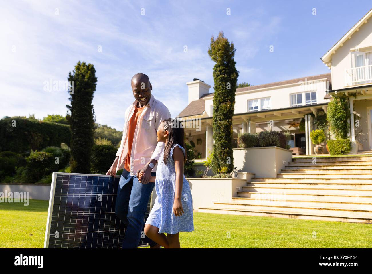 Carrying solar panel, father and daughter smiling and walking in front ...